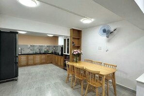 Cozinha moderna com área de jantar, armários de madeira, geladeira preta e ventilador fixado na parede.