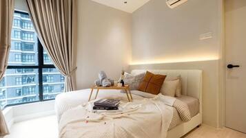 Quarto com cama, mesa de cabeceira, janela com cortinas e vista para edifícios.