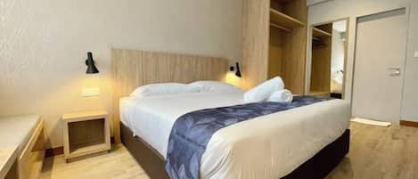 Quarto com cama, mesas de cabeceira, guarda-roupa e espelho.
