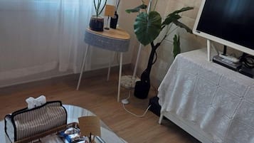 Uma sala de estar com sofá, mesa de centro, televisão e planta em vaso.