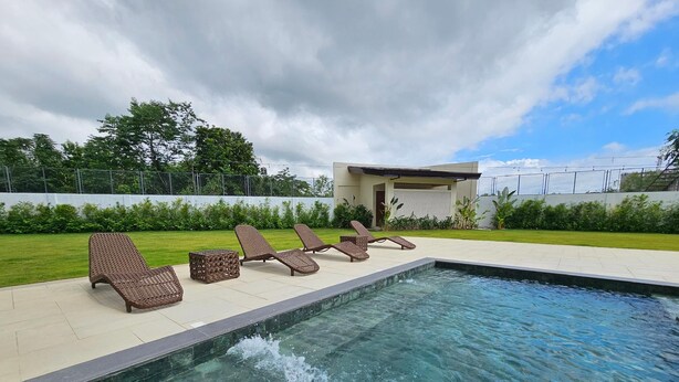 Piscina com espreguiçadeiras e um pequeno edifício ao fundo.