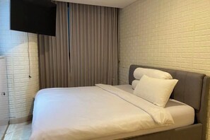Quarto de hotel com cama, cortinas, televisão de tela plana na parede e parede com padrão de tijolos.