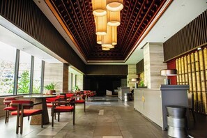 Um hall de hotel moderno com área de estar central, balcão de recepção e vista para o exterior.