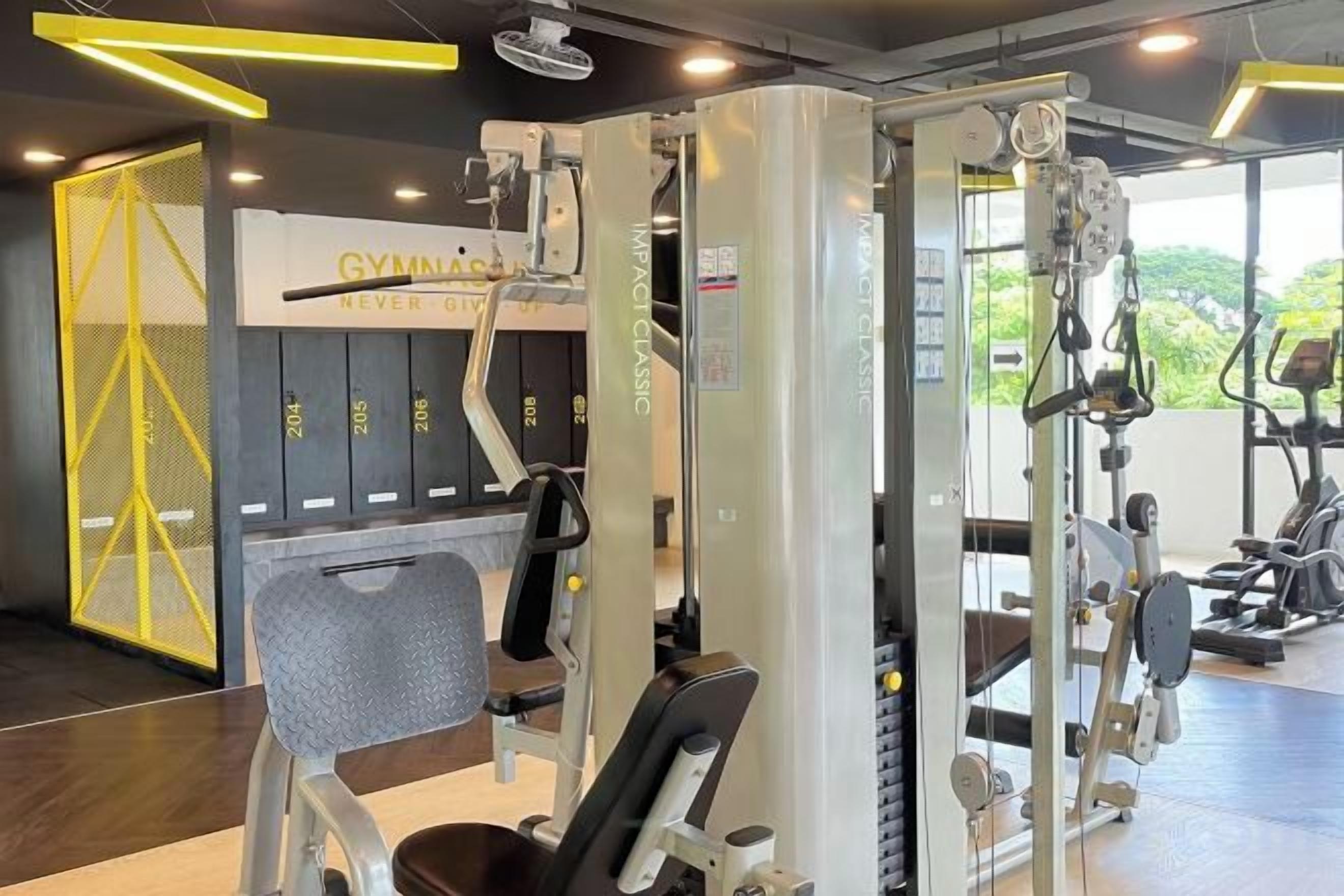 Academia com equipamentos de ginástica, armários e vista para o verde lá fora.