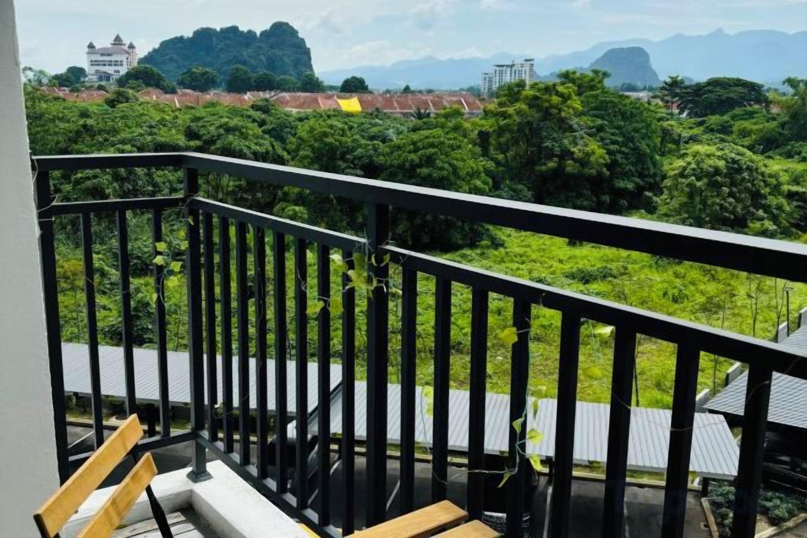 Varanda com guarda-corrimão preto, banco de madeira e vista para vegetação exuberante e edifícios ao longe.