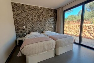Quarto com duas camas, parede estampada e vista para uma parede de pedra e árvores.