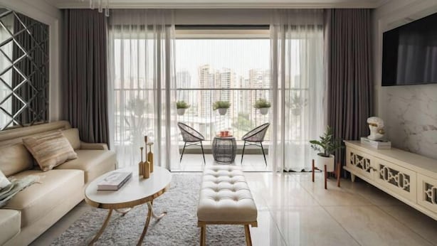 Uma sala de estar moderna com sofá, mesa de centro, um banco e varanda com cadeiras e plantas.