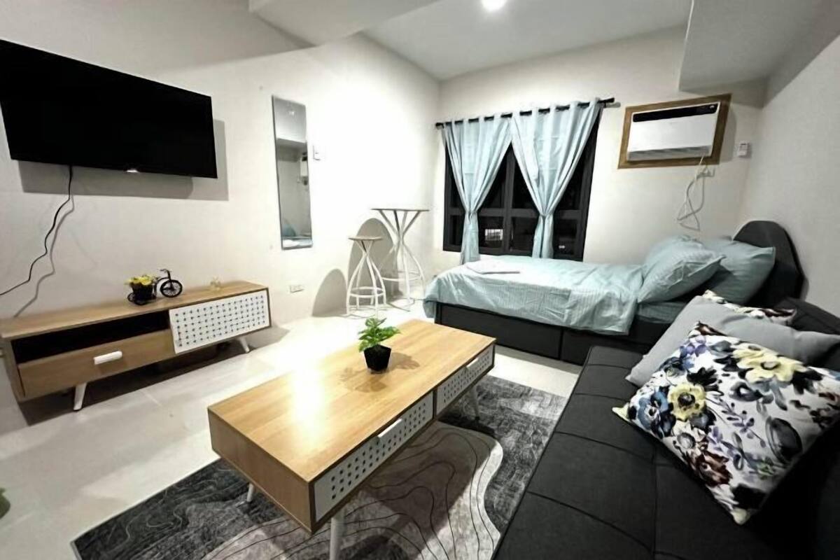 Um quarto moderno com cama, sofá, televisão e uma mesinha com uma planta.