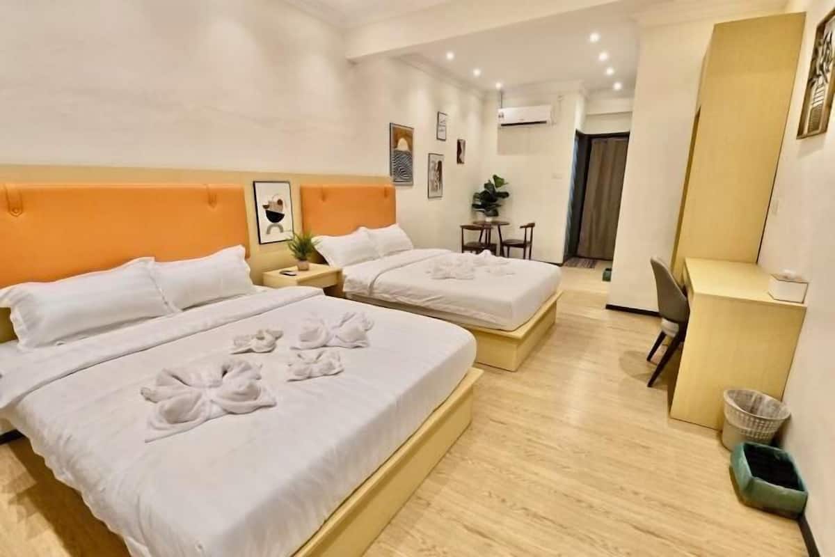 Quarto de hotel com duas camas, uma escrivaninha e um pequeno espaço para sentar.