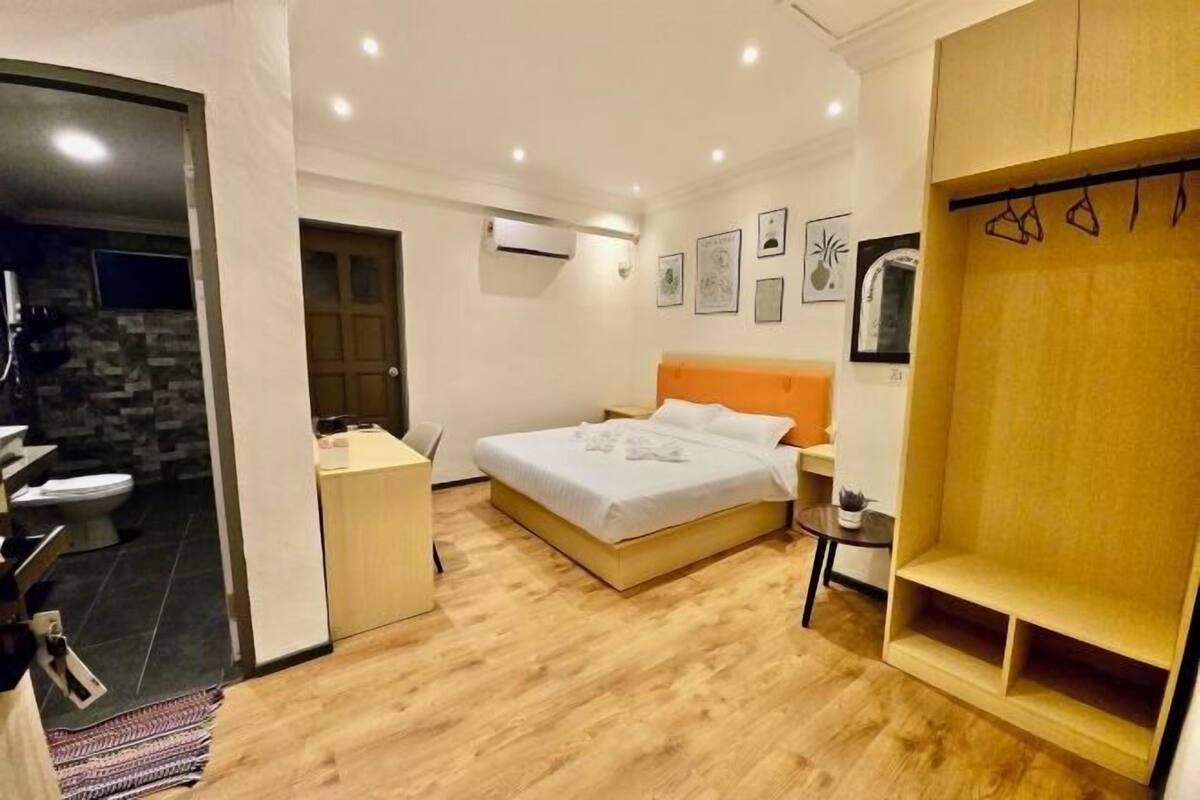 Quarto com cama, escrivaninha, guarda-roupa e banheiro visível por uma porta aberta.
