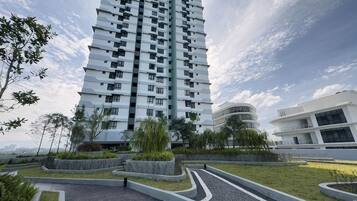 Um moderno edifício alto com estrutura curva, cercado por áreas ajardinadas com caminhos e vegetação.