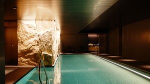 Uma piscina com paredes de pedra, escada de metal e chão revestido de azulejos.