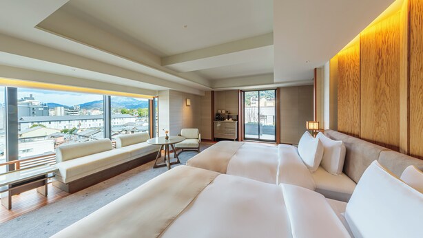 Quarto de hotel moderno com uma cama grande, um sofá, uma mesa pequena e vista para a cidade.