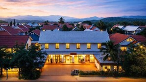Um hotel com um edifício principal e várias estruturas menores, rodeado por vegetação e montanhas ao fundo.
