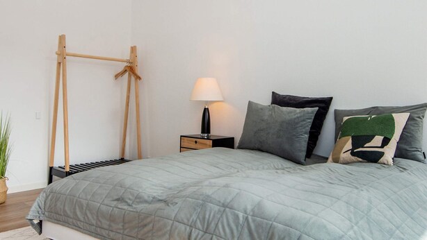 Quarto com cama, mesa de cabeceira, luminária e uma escada de madeira encostada na parede.