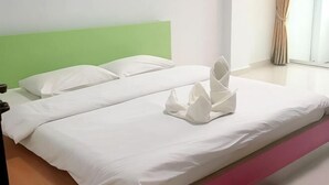 Uma cama de casal com roupa de cama branca, cabeceira verde e mesa de cabeceira com abajur.