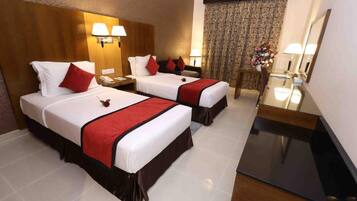 Quarto de hotel com duas camas, uma escrivaninha, um espelho e uma janela com cortinas.