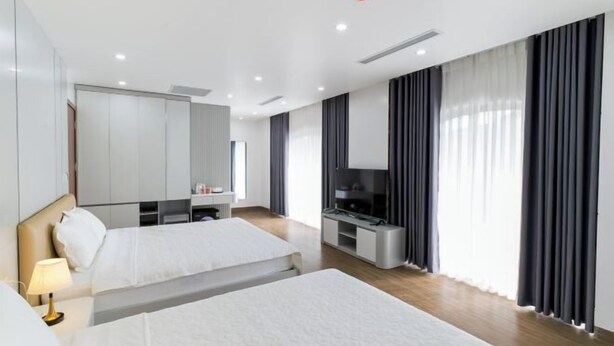 Quarto de hotel moderno com duas camas, televisão, escrivaninha e uma janela grande com cortinas.