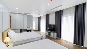 Quarto de hotel com duas camas, televisão, escrivaninha e uma janela grande com cortinas.