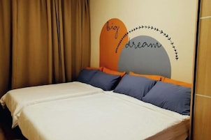 Cama com roupa de cama branca, almofadas azuis e parede com um desenho circular e texto.