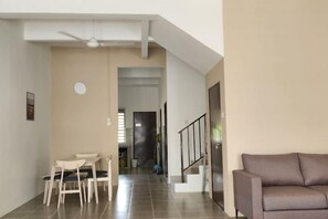 Uma sala de estar com sofá, uma mesa de jantar com cadeiras e uma escada que dá acesso a outro andar.