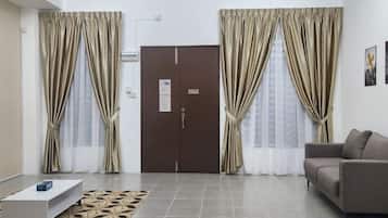Quarto com sofá, mesa de centro, cortinas, porta e tapete estampado.