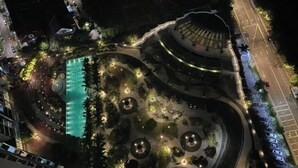 Vista aérea de uma área ajardinada com jardins circulares, uma piscina central e um edifício redondo com cúpula.