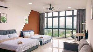 Quarto de hotel com duas camas, um sofá, uma escrivaninha, um ventilador de teto e janelas amplas com vista.