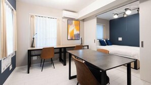Quarto de hotel moderno com área de refeições, cama e uma janela grande.