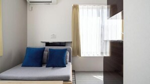 Quarto com cama, ar condicionado, janela com cortinas e uma pequena mesa.