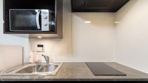 Uma cozinha com micro-ondas embutido, pia de aço inoxidável e bancada preta.