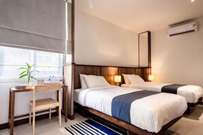Quarto de hotel com duas camas, uma escrivaninha, uma cadeira, uma janela grande e um aparelho de ar condicionado.