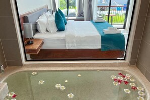 Quarto de hotel com cama, banheira com flores e vista para piscina e edifício.