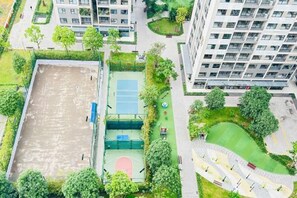 Vista aérea de uma área residencial com quadra de basquete, quadra de tênis e um parque arborizado.