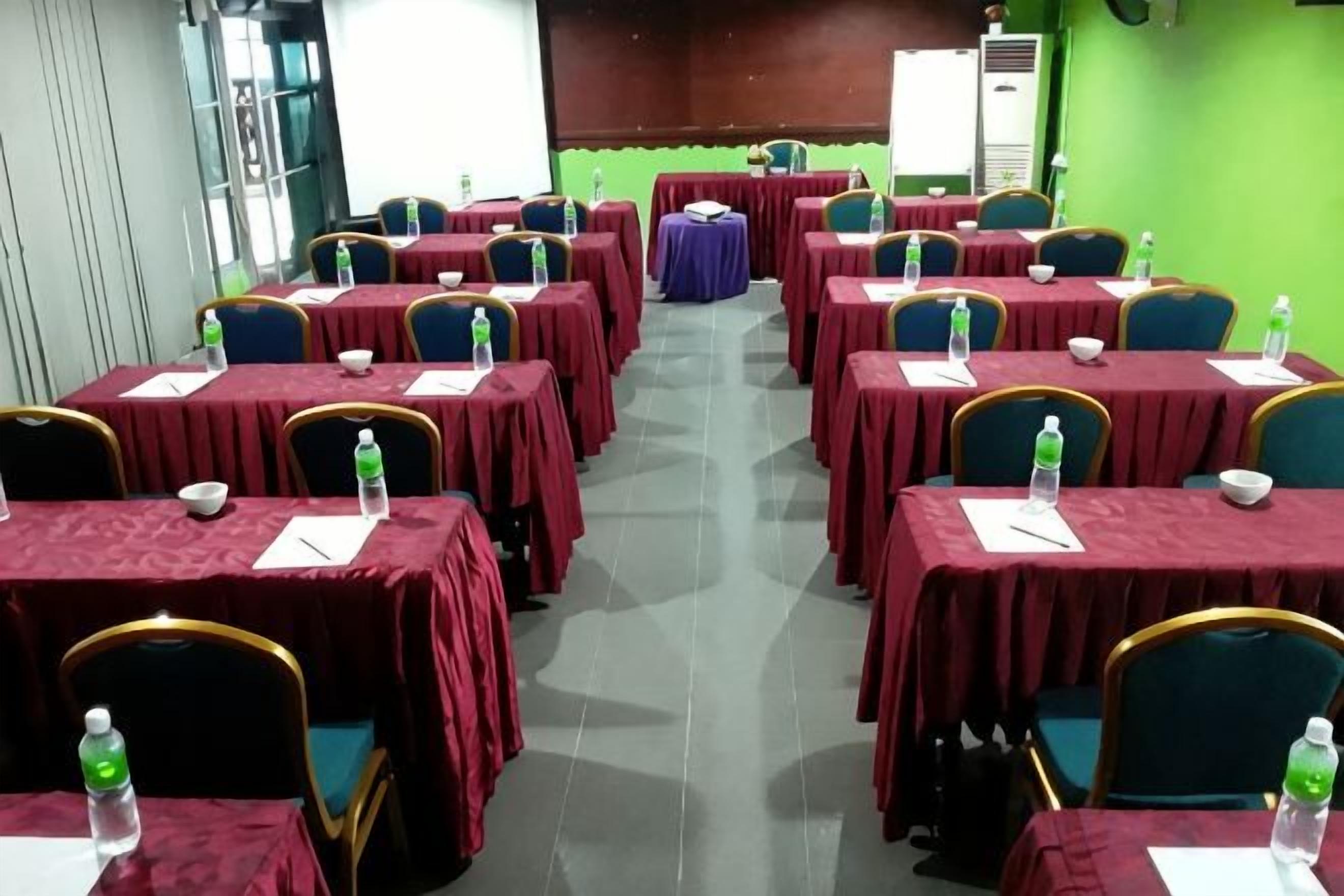Sala de conferência com várias mesas, cada uma com toalha vermelha, cadeiras e garrafas de água.