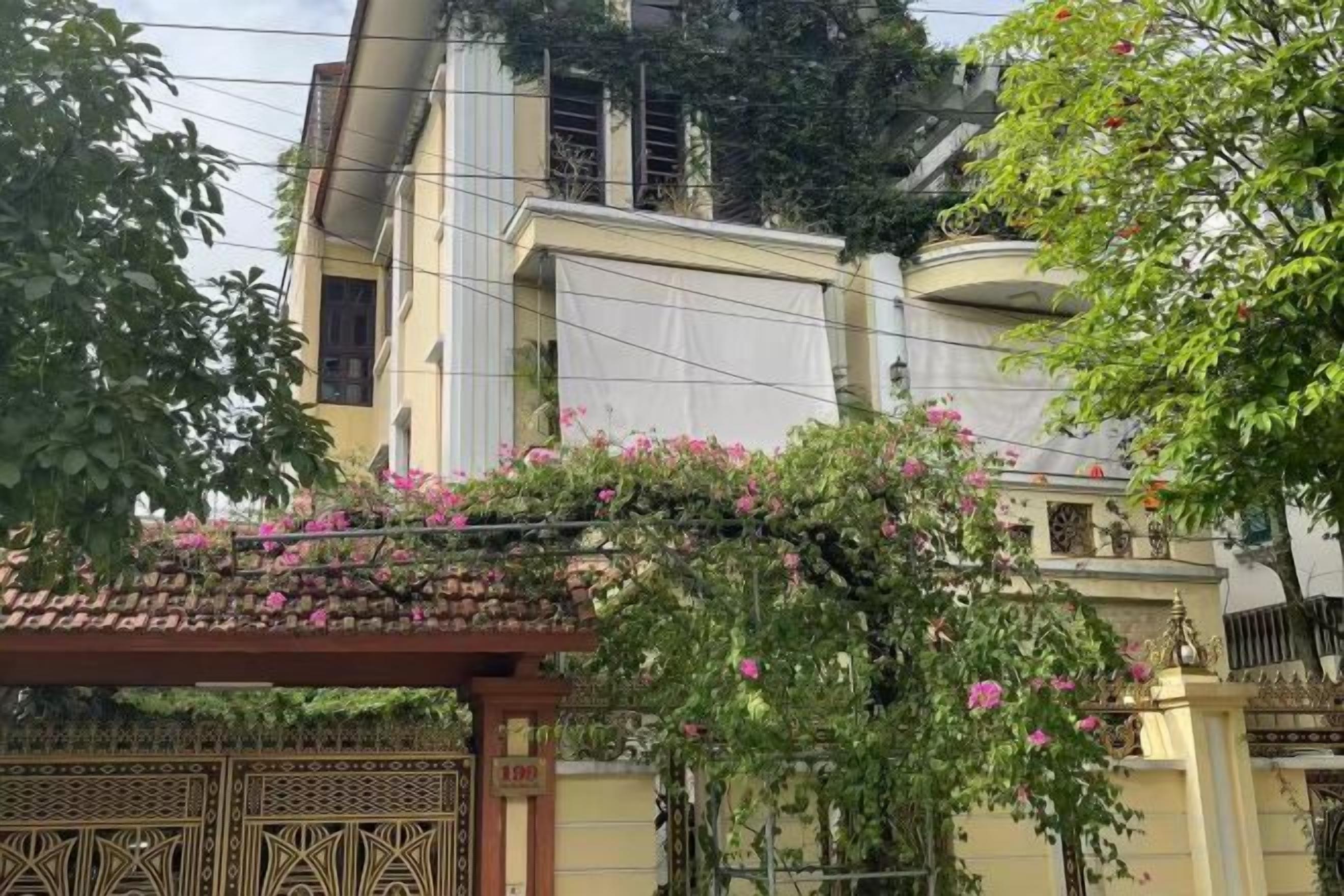 Um prédio residencial com portão fechado, varanda coberta e uma árvore com flores cor-de-rosa.