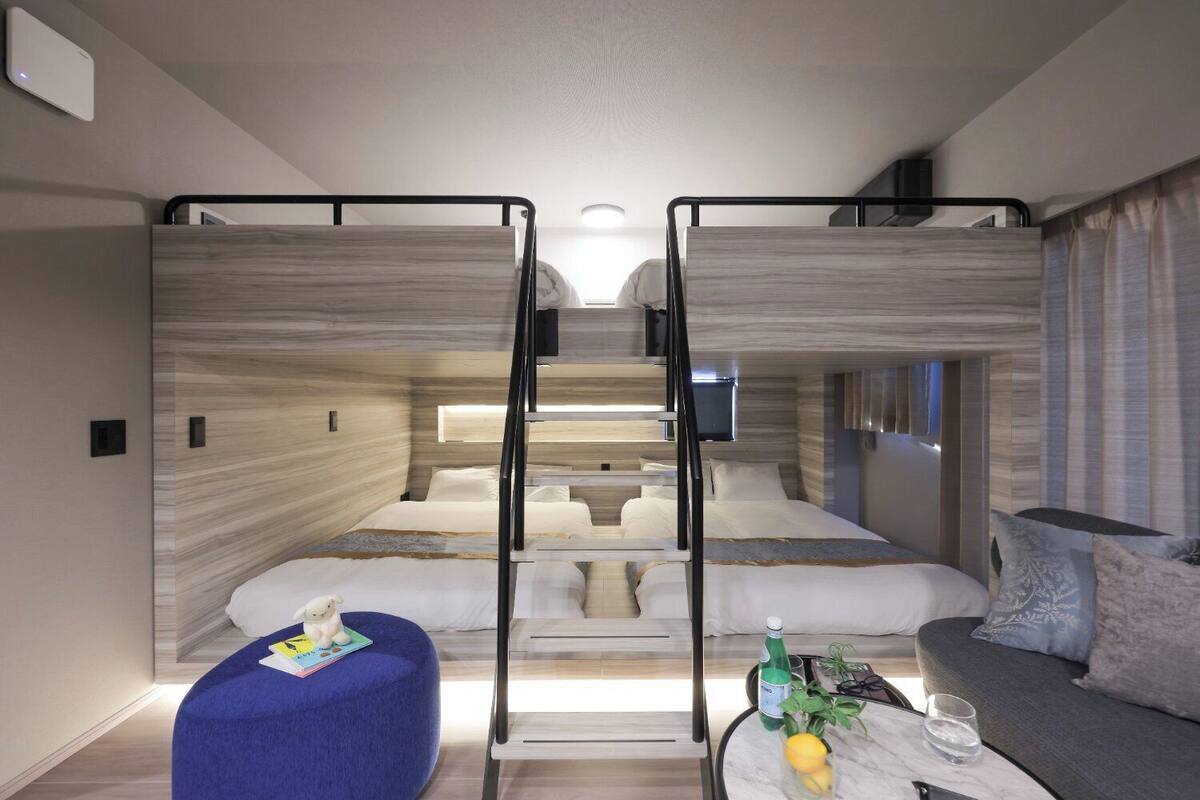 Quarto compacto e moderno com beliches, uma mesinha com bebida e livro, e um sofá com almofadas.