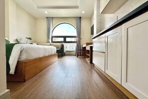 Quarto de hotel com chão de madeira, uma cama grande, uma escrivaninha e uma janela com cortinas.