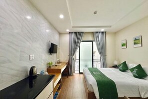 Quarto de hotel com cama, escrivaninha, televisão e varanda com cortinas.