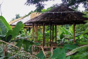 Uma estrutura tradicional de gazebo em bambu, rodeada por vegetação exuberante.