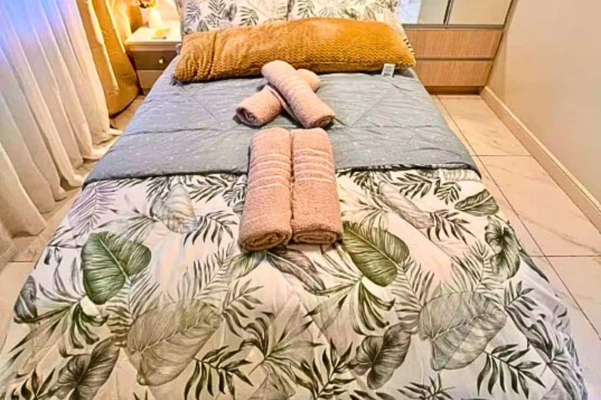 Quarto com cama, mesa de cabeceira, espelho e porta.