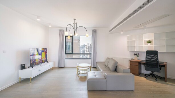 Uma sala de estar moderna com sofá branco, televisão, mesa de jantar e vista para a cidade através de grandes janelas.