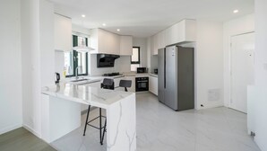 Uma cozinha moderna com armários brancos, uma ilha de mármore, eletrodomésticos de aço inoxidável e iluminação embutida no teto.