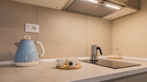Cozinha com uma chaleira azul, uma cafeteira e duas chávenas numa bancada.