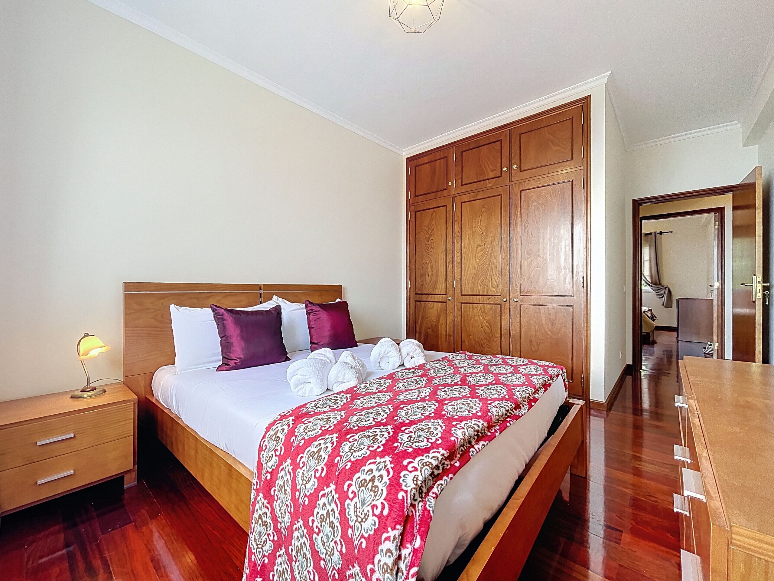 Quarto de hotel com cama de madeira, mesa de cabeceira, guarda-roupa e espelho.