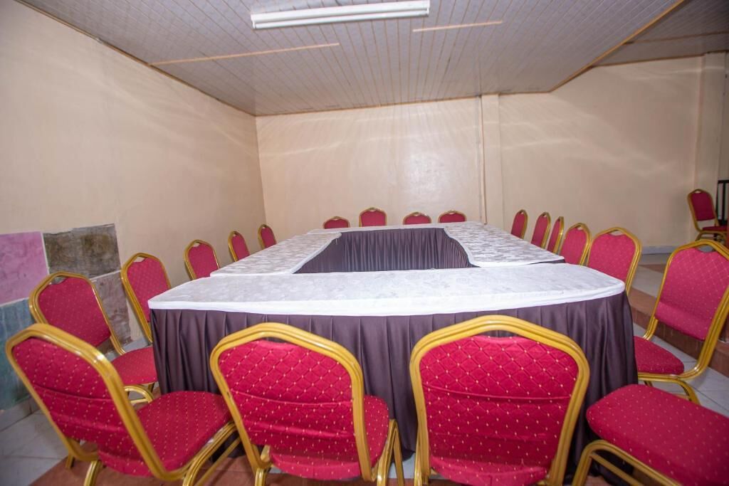 Uma sala de conferências com uma mesa redonda, cadeiras estofadas em vermelho e toalha de mesa branca.