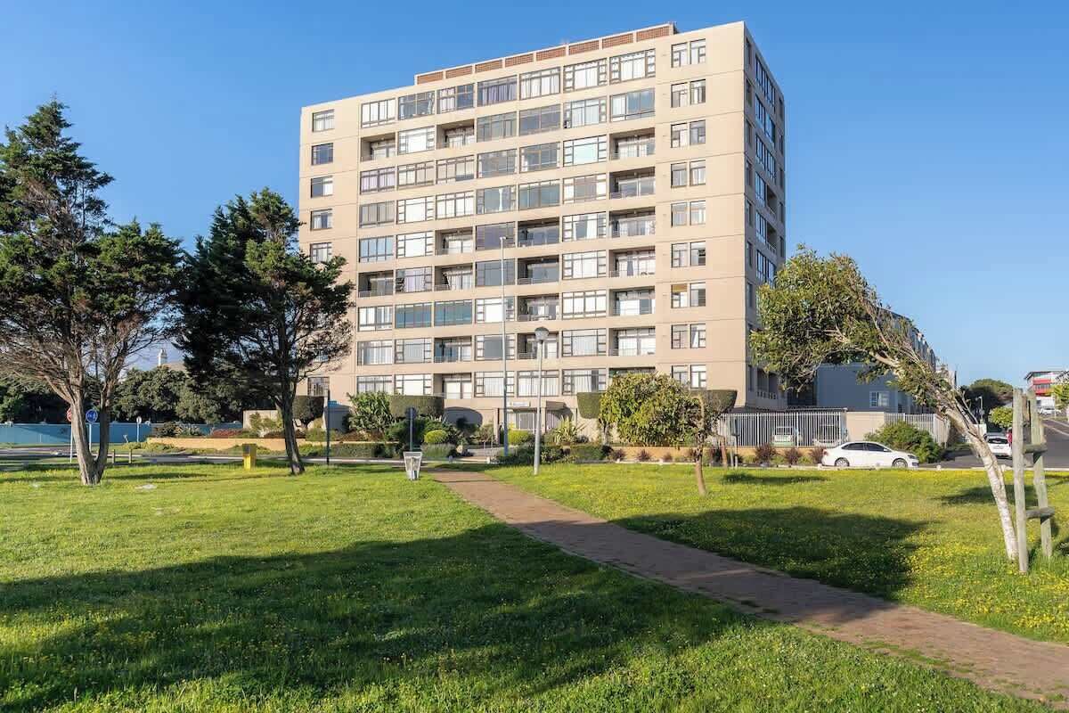 Edifício residencial de vários andares com fachada plana, grandes janelas e um pátio ajardinado com árvores.