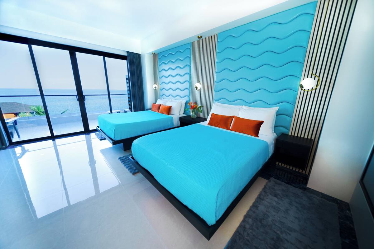 Quarto de hotel moderno com uma cama grande, uma cama menor e uma varanda com vista para o mar.