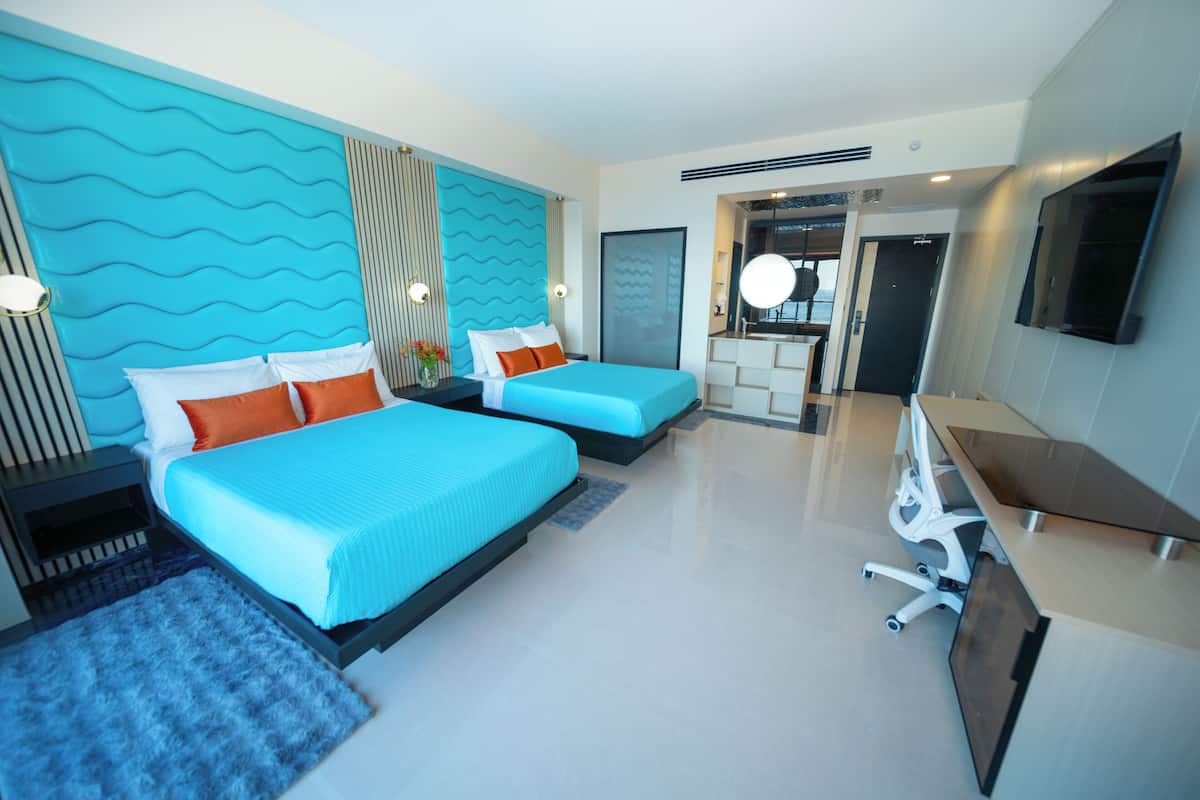 Quarto de hotel moderno com duas camas, uma escrivaninha e um banheiro.