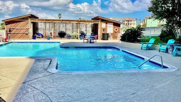 Piscina com deck de madeira, cadeiras de descanso e área coberta com uma placa.